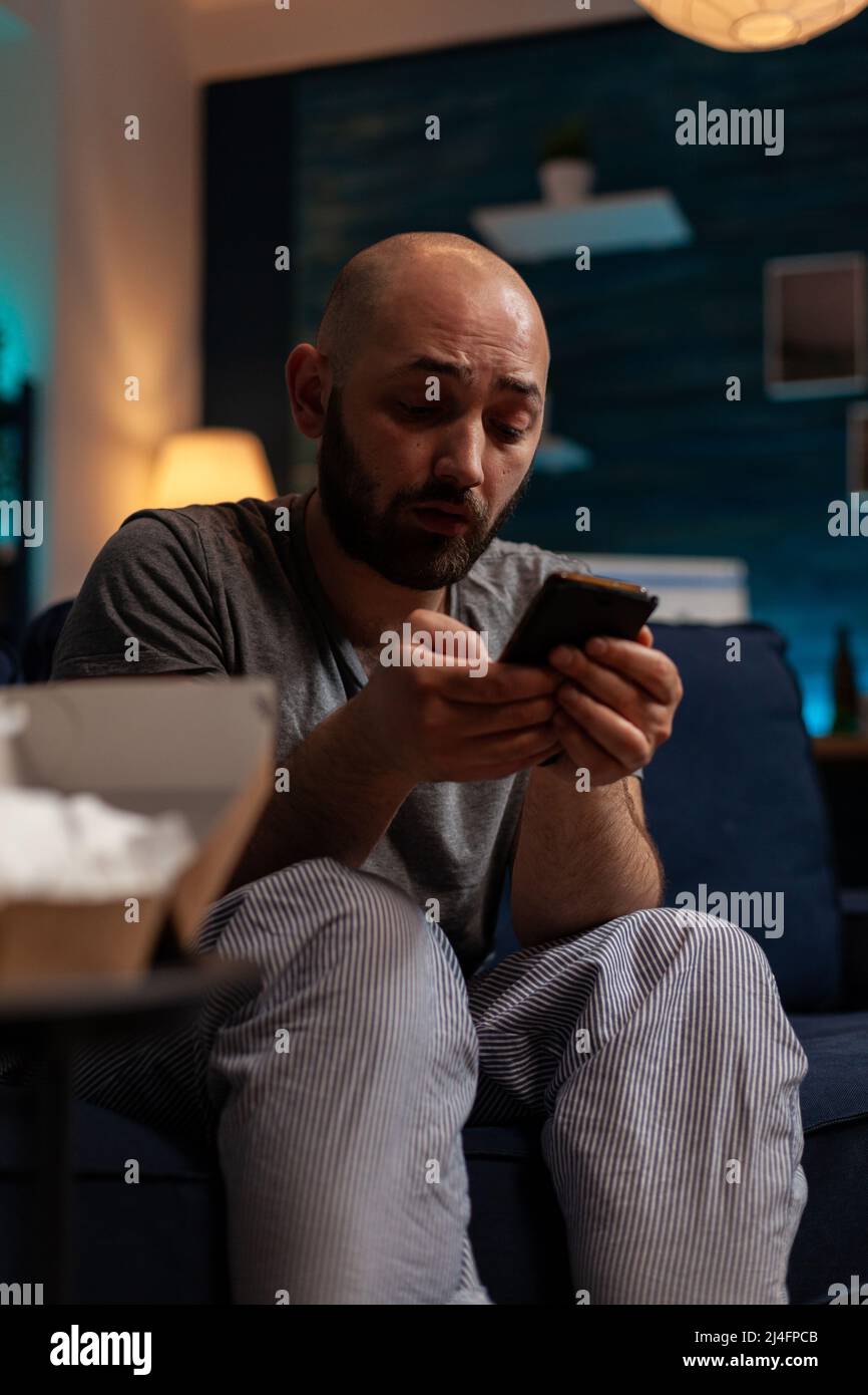 Depressed man using smartphone to browse internet at home, trying to ...