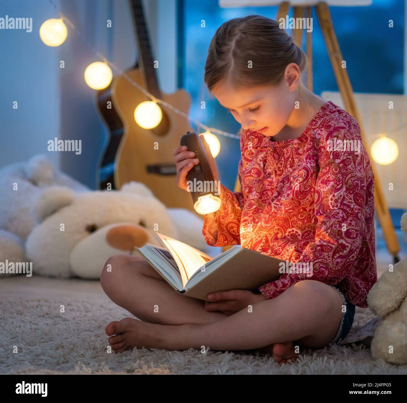 Cute little girl reading book at night using flashlight indoors Stock ...