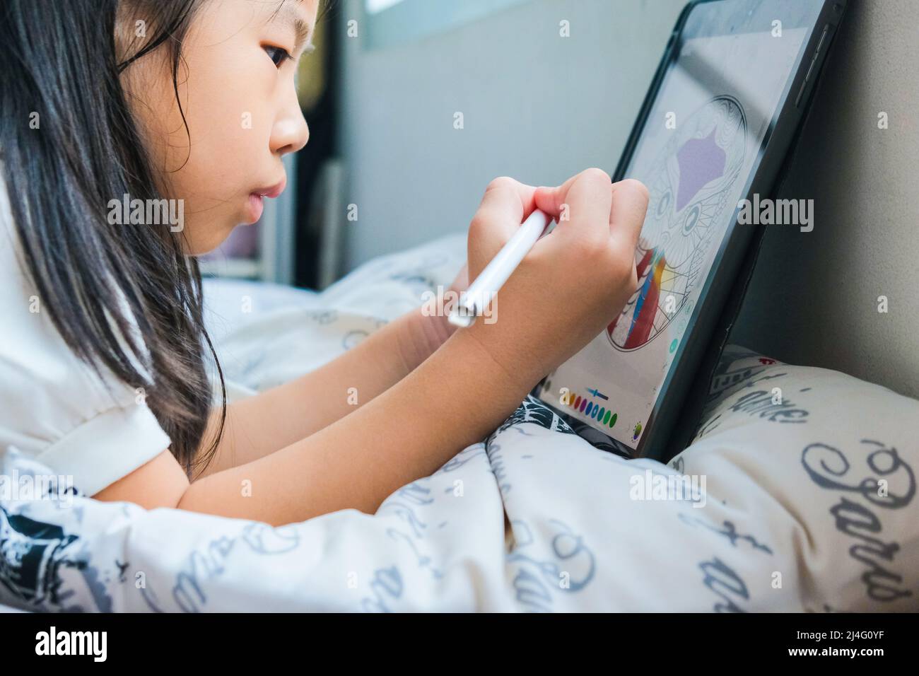 Little kid girl intend to drawing cartoon with tablet lying on bed art ...