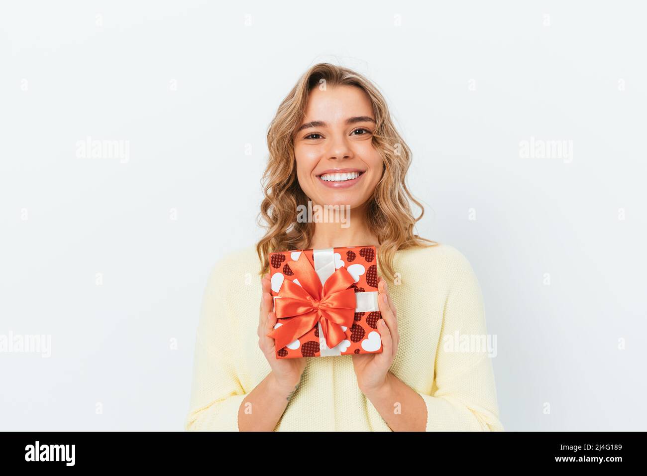 Happy young woman holding gift box smiles and looking at camera, white ...