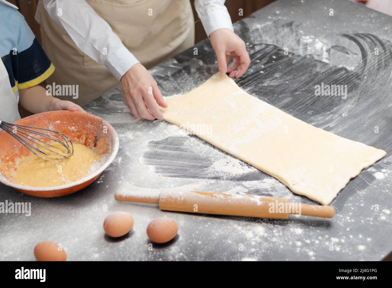 The female hands of the cook roll out puff pastry for baking on a black ...