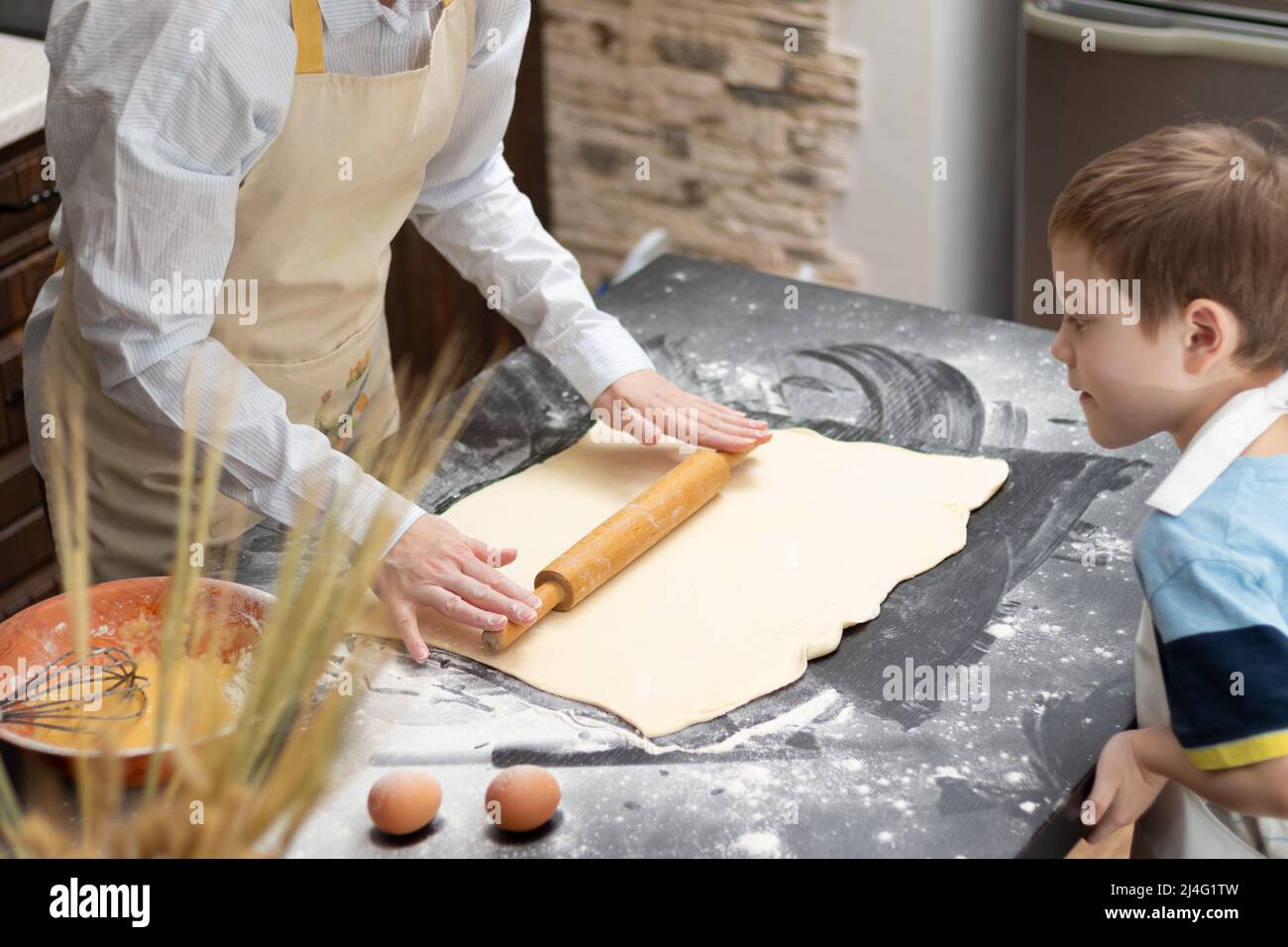 Mom and son in aprons roll out puff pastry for baking on a black ...