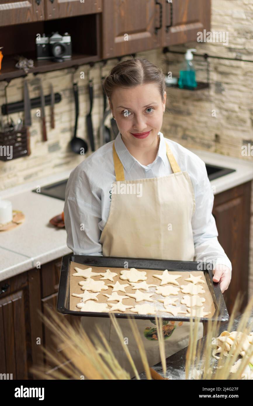 A young pretty woman cook in an apron holds a baking sheet with puff ...