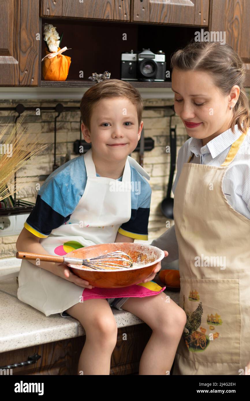 Beautiful young mom cook in an apron with her son prepares cookie dough ...