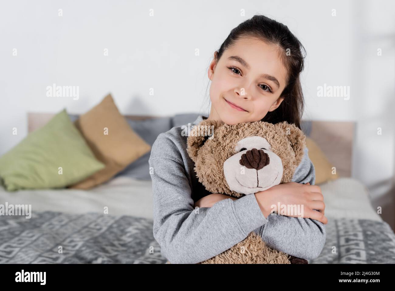 cheerful preteen girl embracing teddy bear and looking at camera in ...