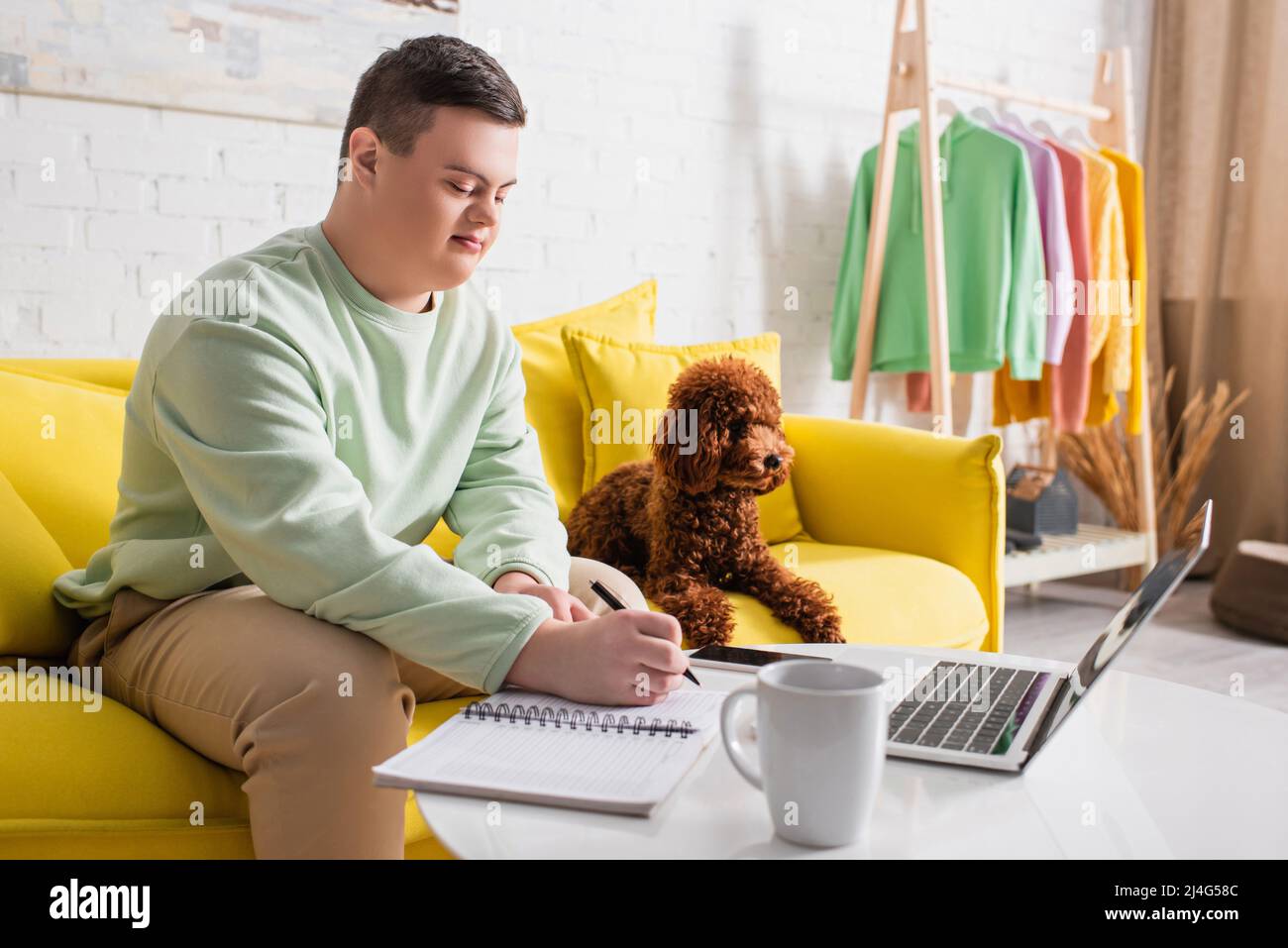 Teenage boy with down syndrome writing on notebook near poodle and ...