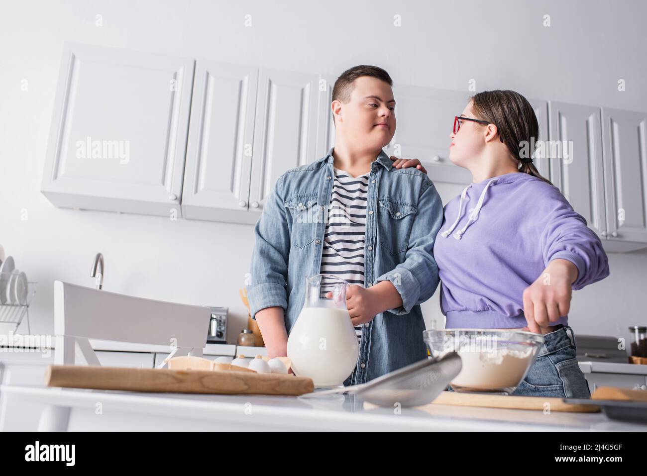 Low angle view of teenager with down syndrome cooking near boyfriend at ...