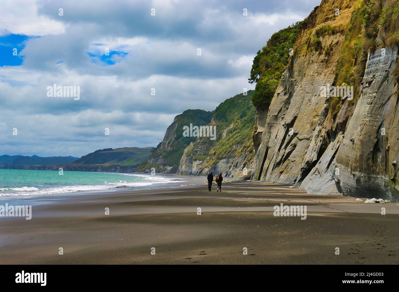 Two people walking on a deserted beach with towering limestone cliffs ...