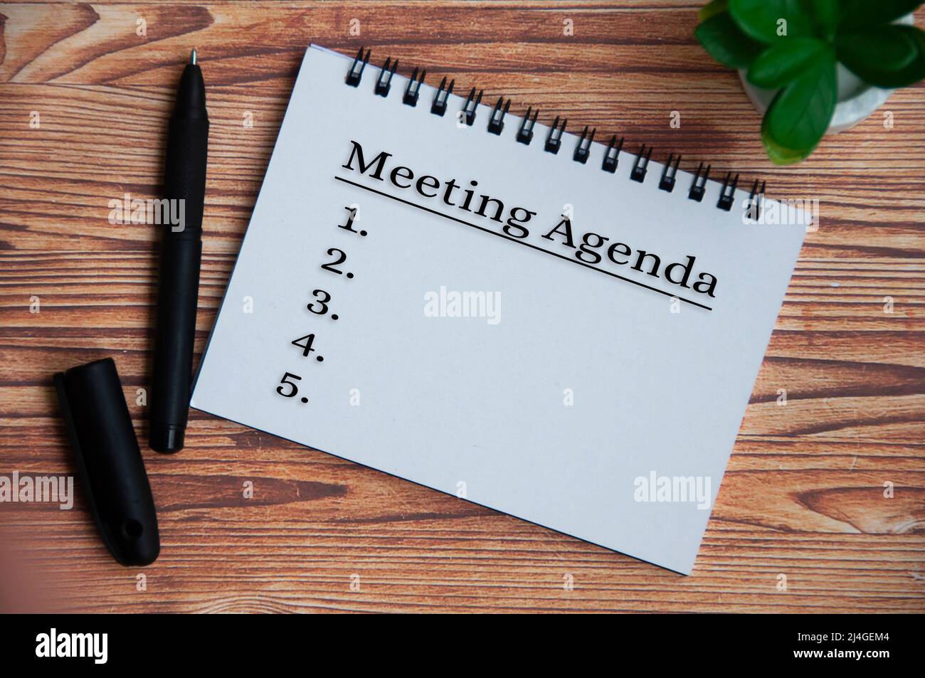 Meeting agenda text on notepad with plant, pen and wooden table ...