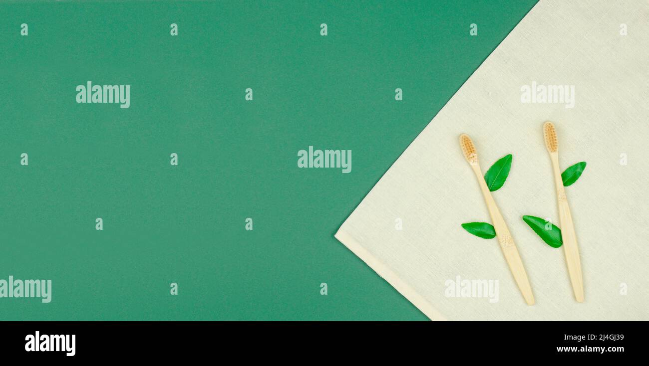 Bamboo toothbrushes with green leaves lie on a linen material. Eco ...