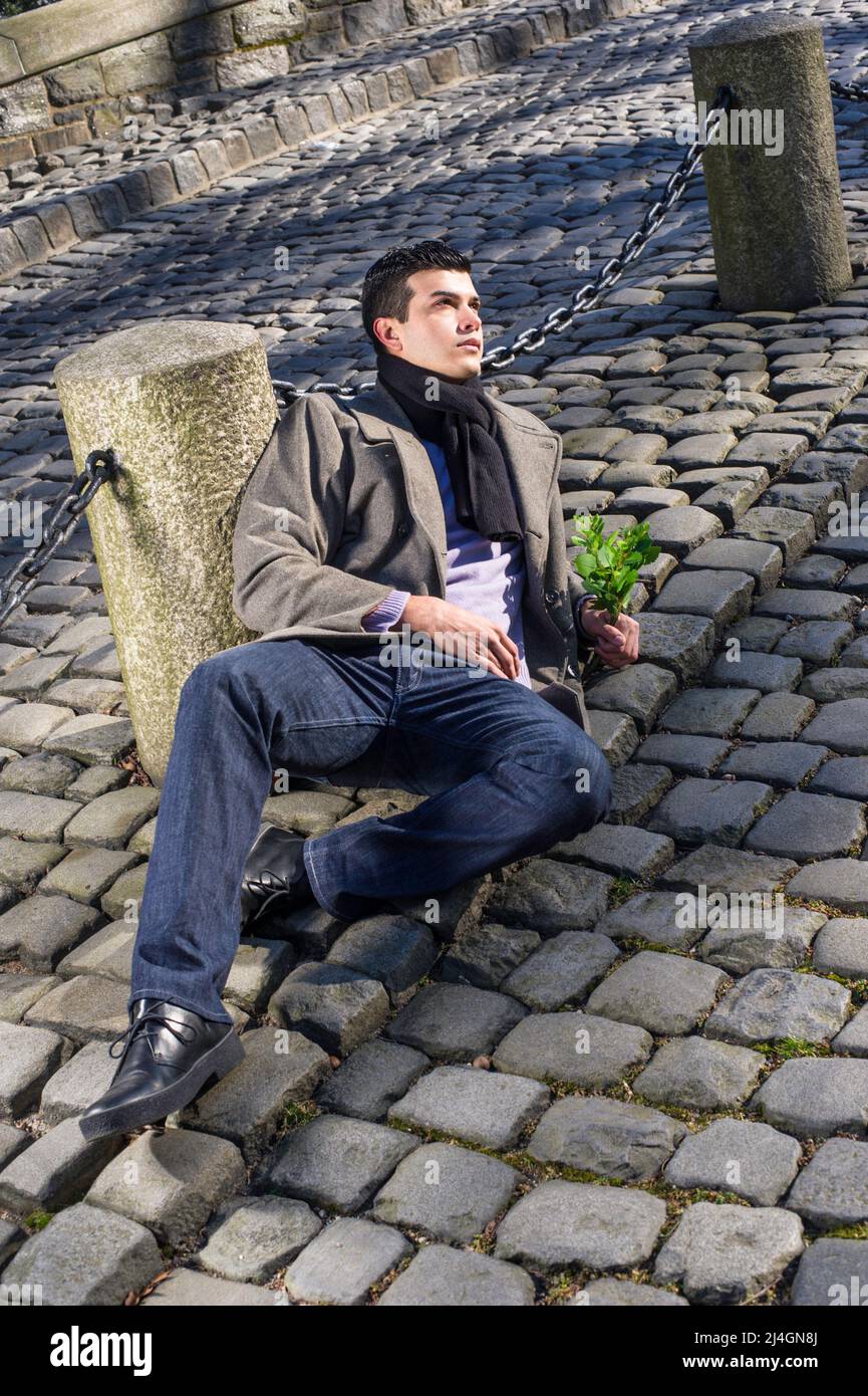 A young guy is lay on the ground, one hand holding a bunch of green ...
