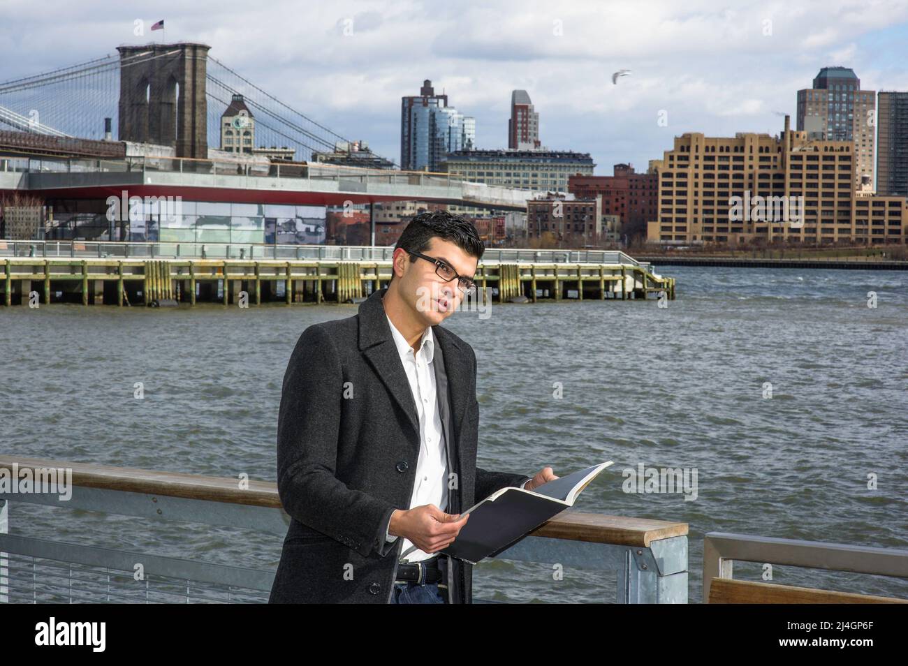 A young handsome scholar is holding a book and standing on a river bank ...