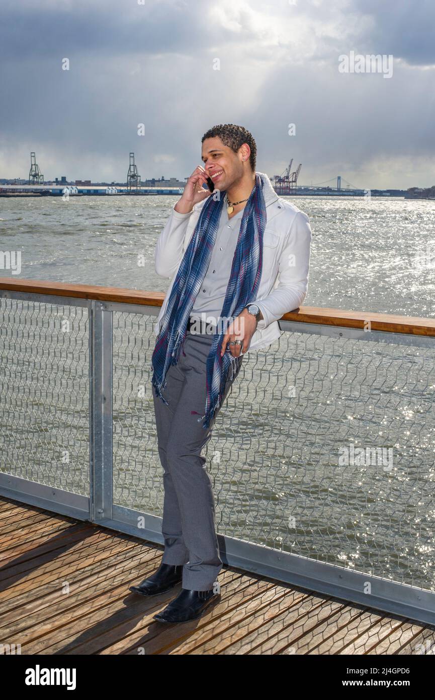 A young guy is standing on the dock, smiling and talking on the phone ...