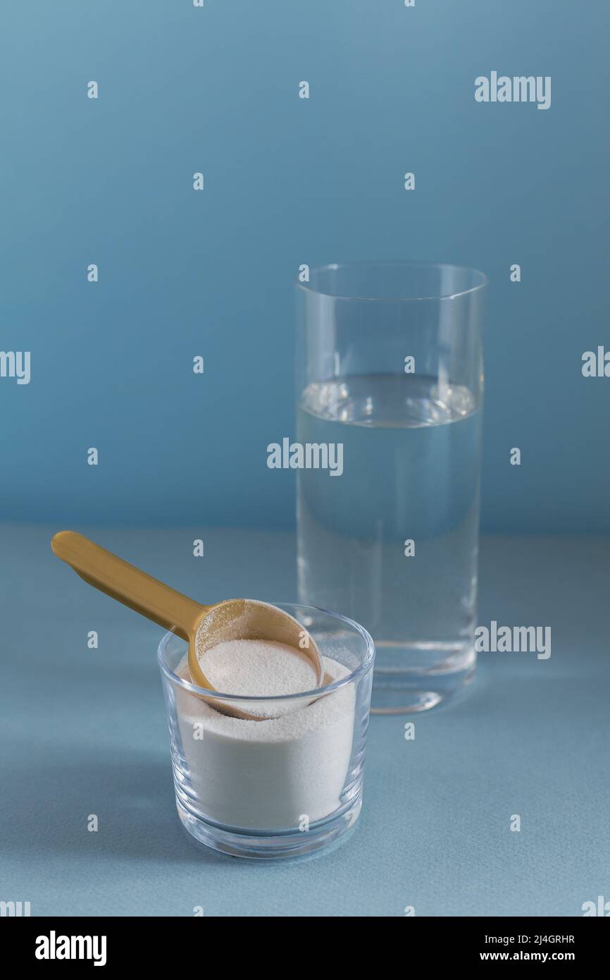 Collagen powder in bowl, glass of water and measure spoon on light blue ...