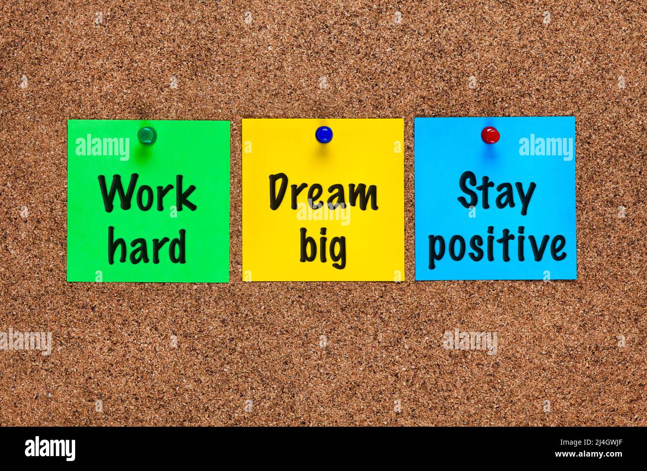 Three colored notes on corkboard with words Work hard, Dream big, Stay ...