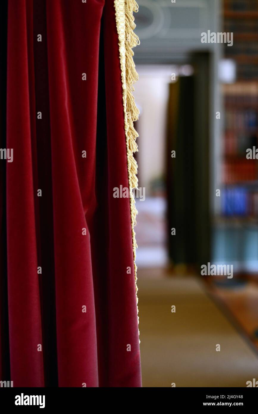 Red velvet curtain drawn open to an old library room Stock Photo - Alamy