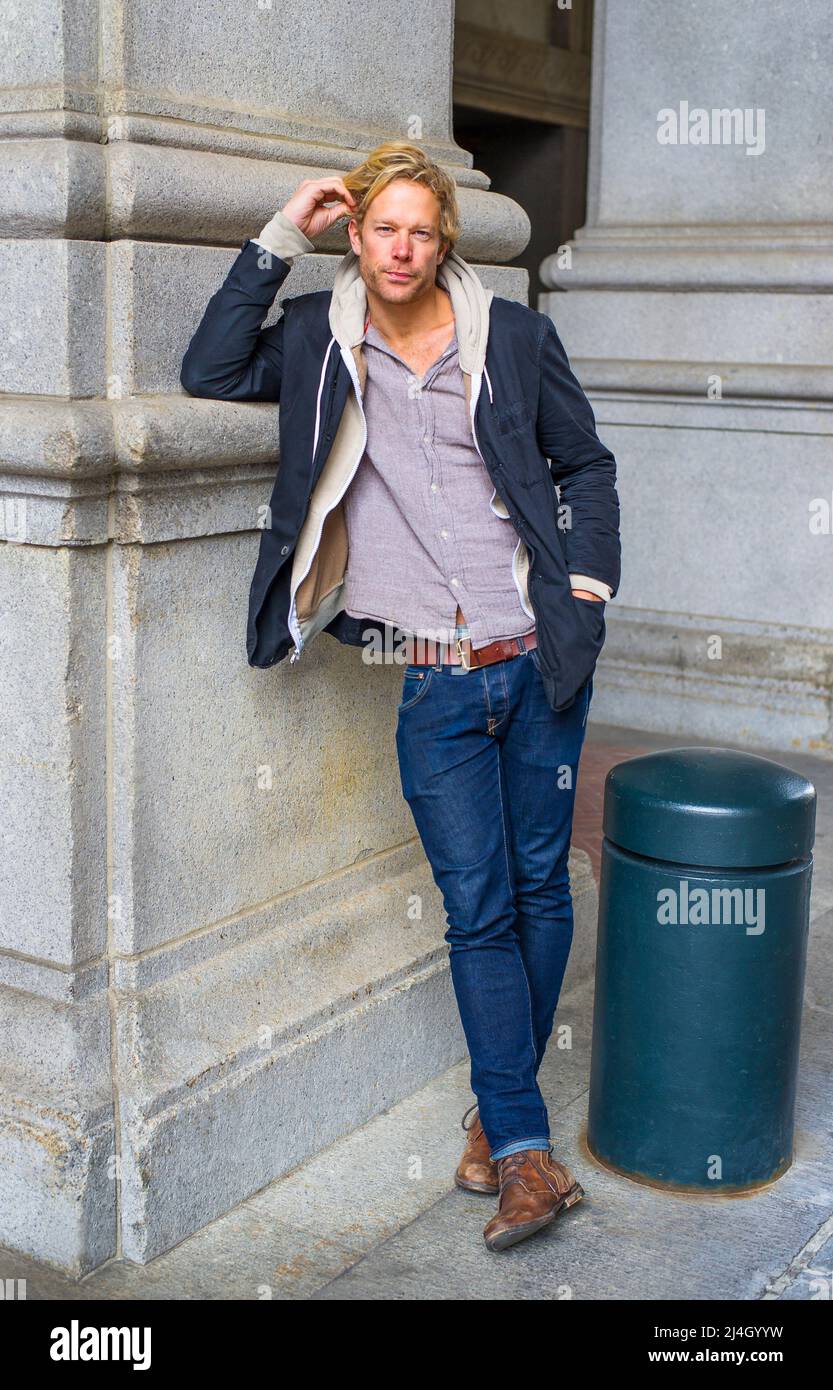 A young handsome guy is standing outside against a column, scratching ...