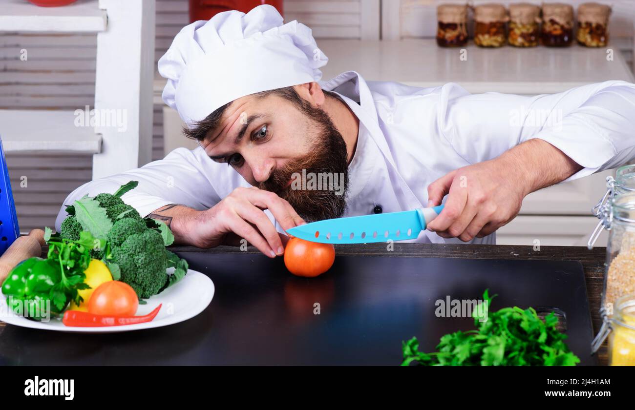 Male chef in white uniform cuts tomatoes with knife. Preparing dishes ...