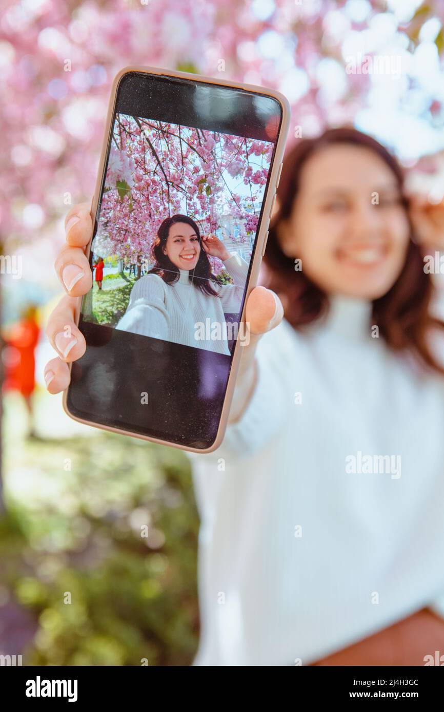 woman shooting her self on the phone under blooming sakura tree selfie ...