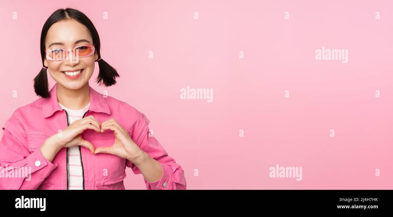 Lovely korean female model in trendy sunglasses, shows heart, care sign ...