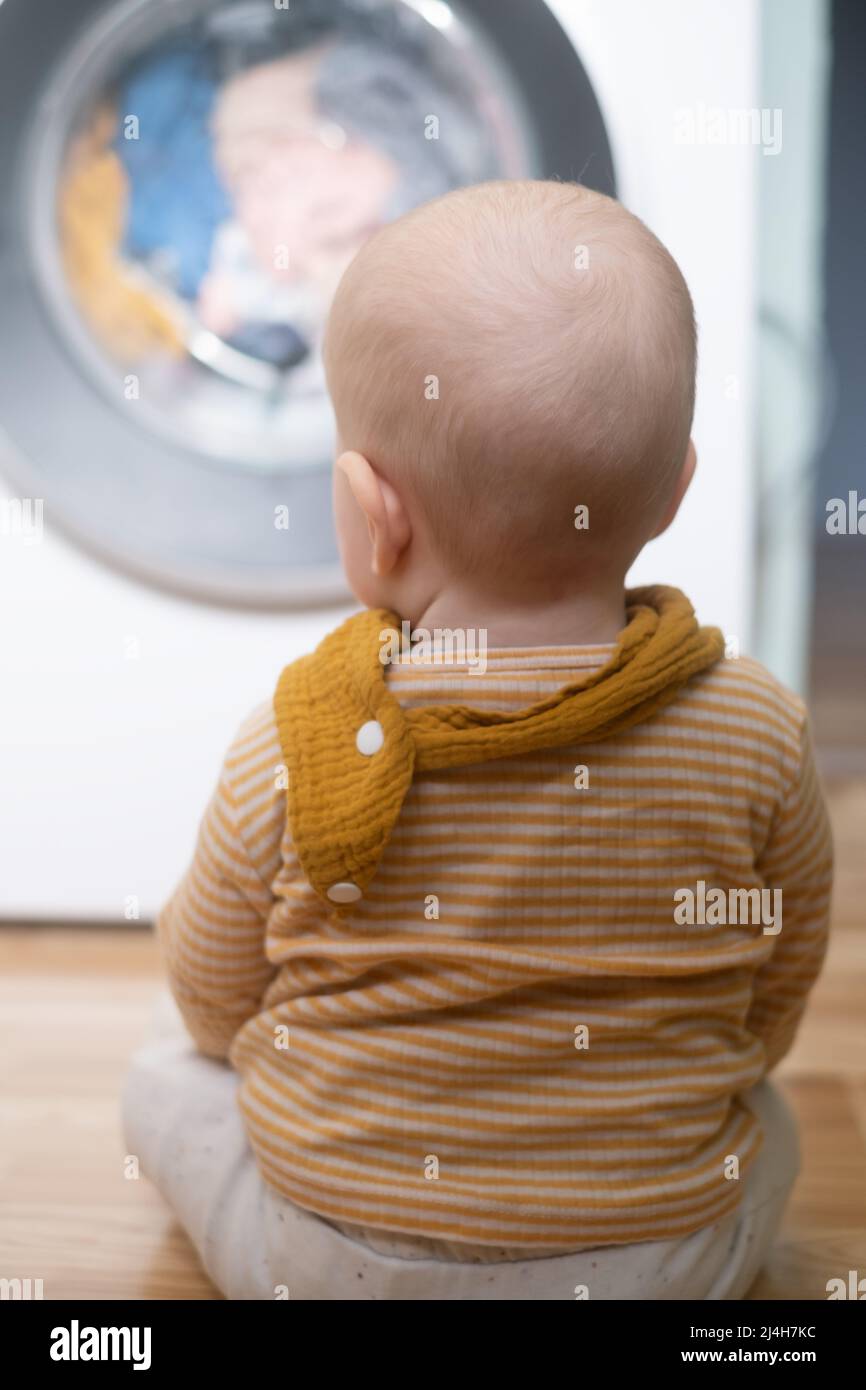 Little curious caucasian girl playing with washing machine watching on ...