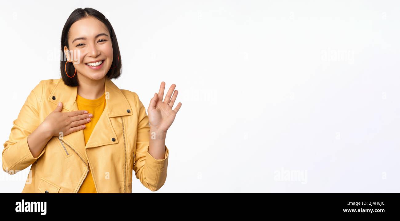 Image of friendly asian girl in stylish yellow coat, raising arm ...