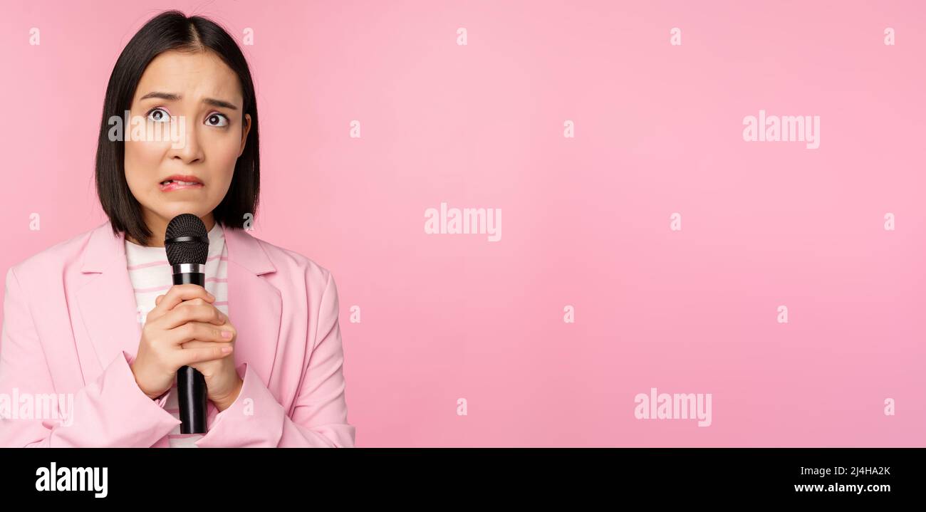 Anxious asian lady in suit, talking in public, giving speech with ...