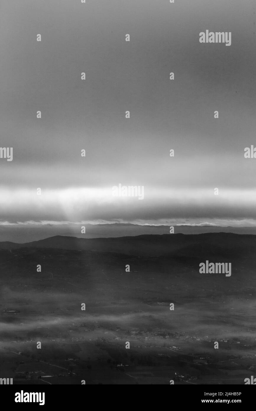 Sun rays coming down from some clouds over a valley filled by fog ...