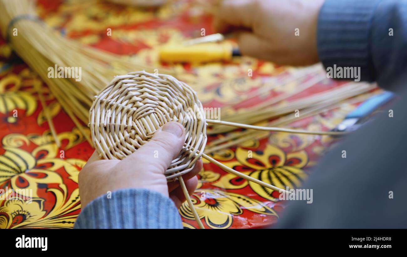 Hands weaving the bottom of a straw basket. ART. A man weaves a round ...