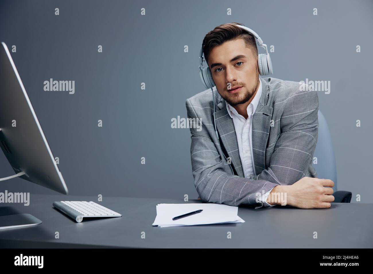 manager in headphones in a gray suit sits in front of a computer ...