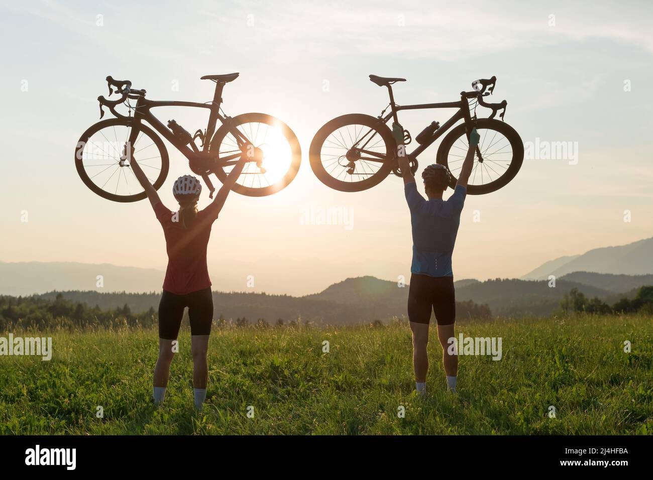 Two cycling racer silhouettes reach the goal and lift bikes above their ...