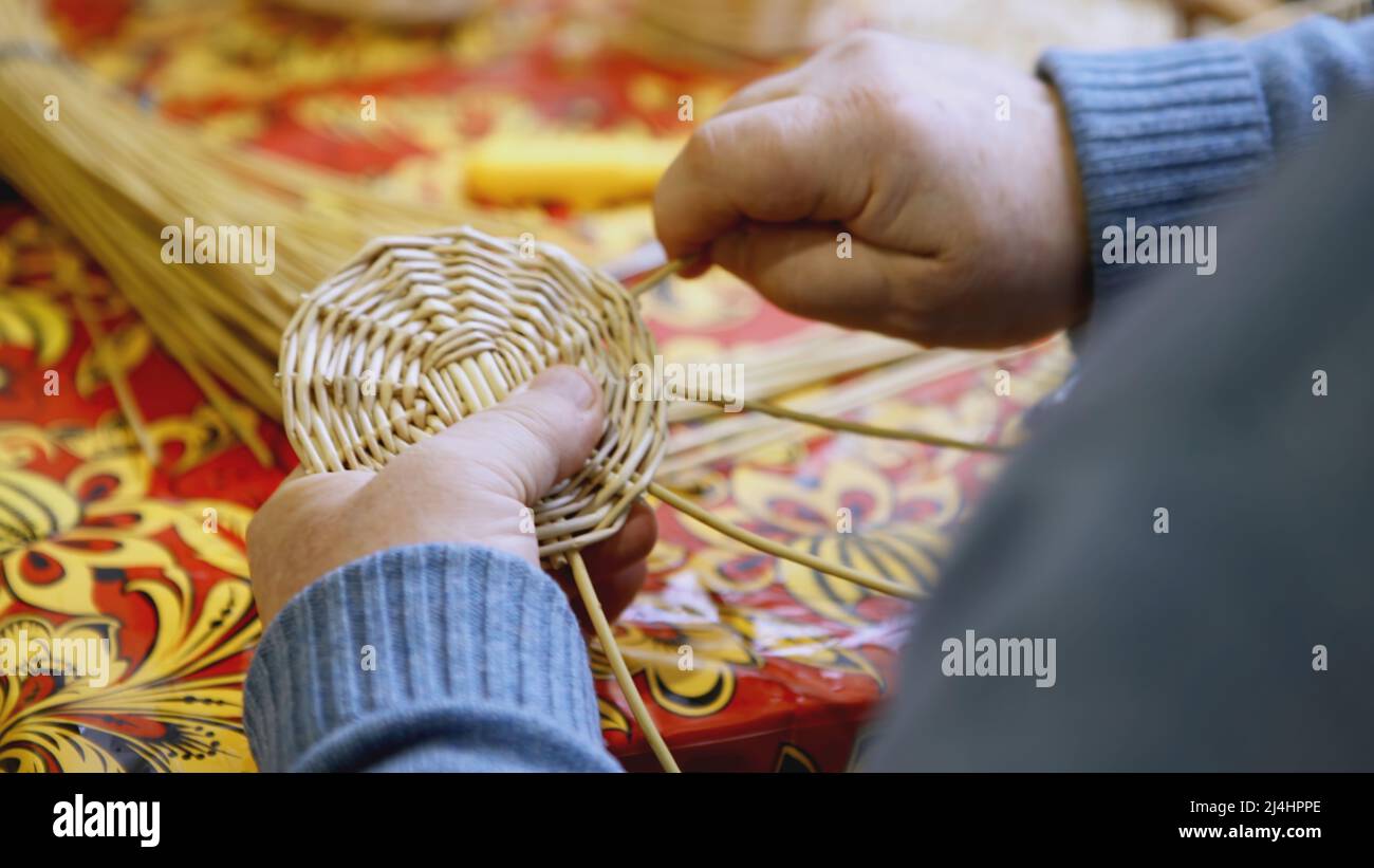Hands weaving the bottom of a straw basket. ART. A man weaves a round ...