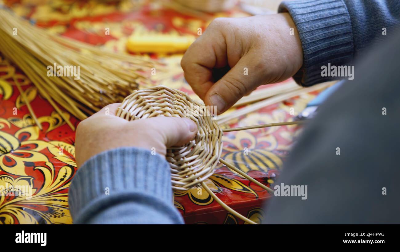 Hands weaving the bottom of a straw basket. ART. A man weaves a round ...