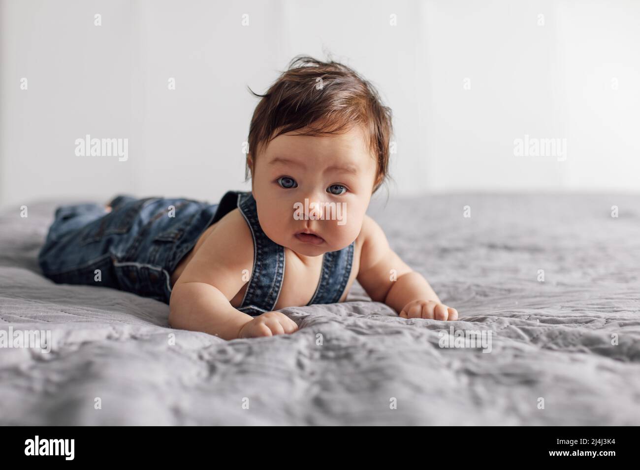 Portrait of scared baby wearing denim romper lying on gray blanket at ... Portrait of scared baby wearing denim romper lying on gray blanket at ...
