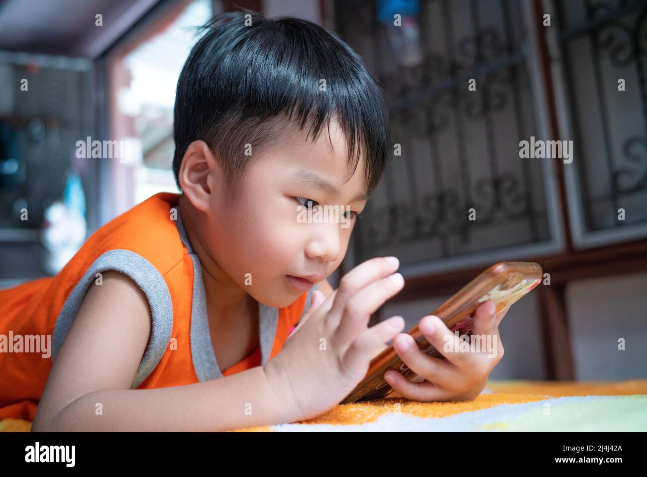 Little boy playing internet communication onn smartphone lying on bed ...