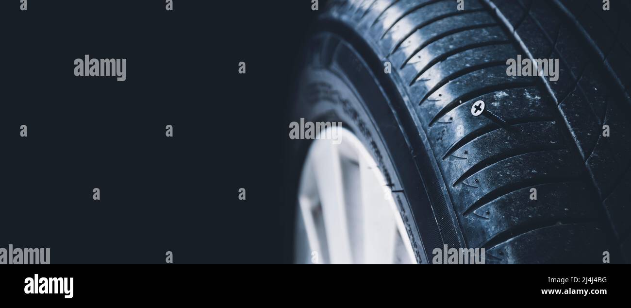 A close-up shows a sharp metal screw piercing an automobile tire,black ...
