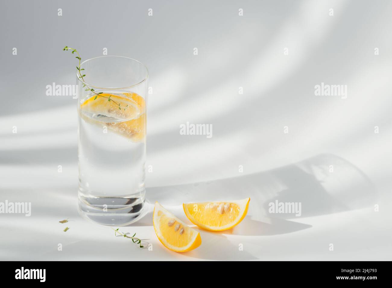 Glass of clean mineral sparkling water with ice and lemon on a white background with sunshine ...