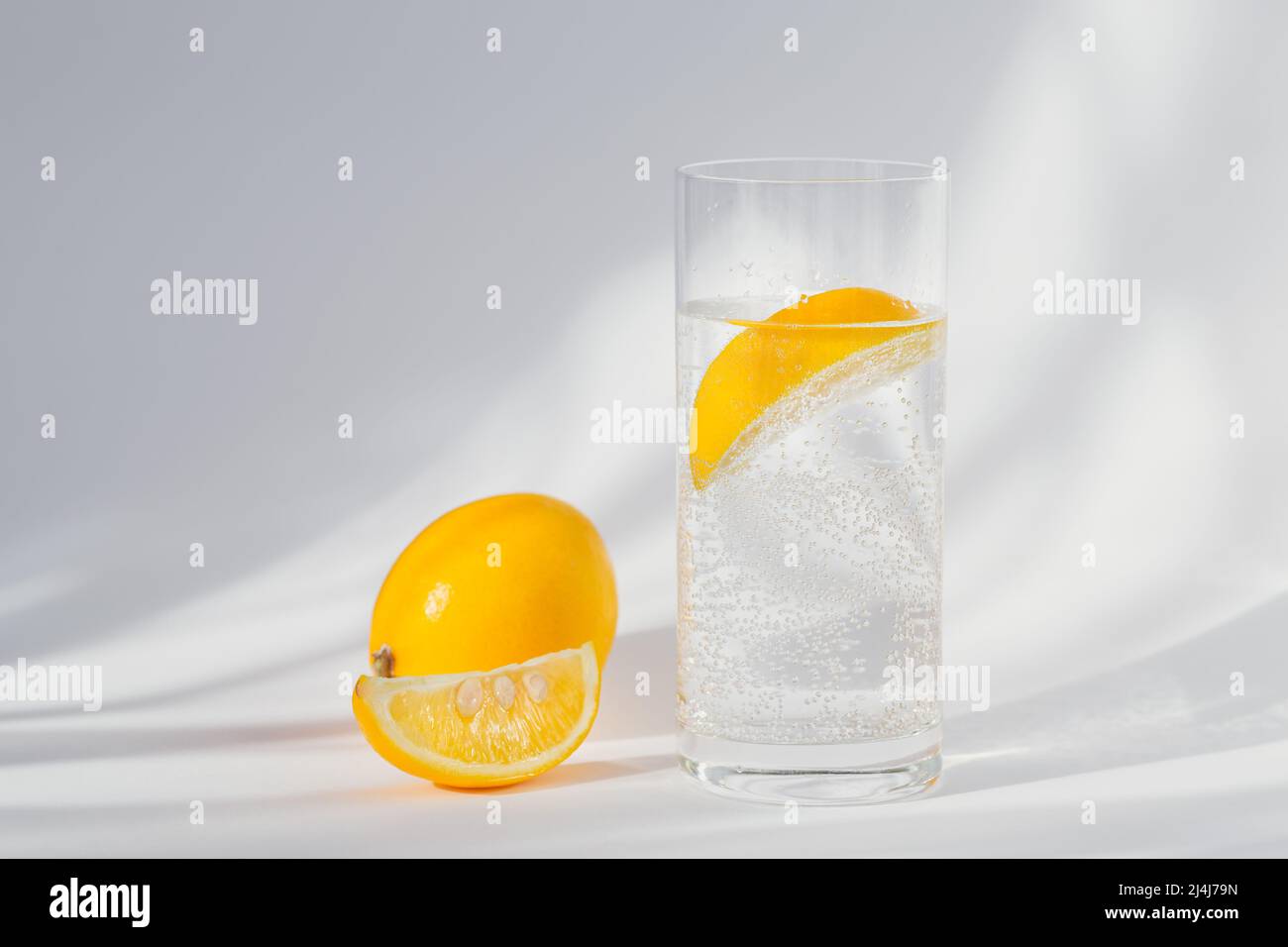 Glass of clean mineral sparkling water with ice and lemon on a white background with sunshine ...