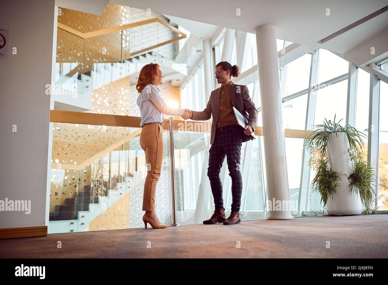A young businessman is hand shaking with a female colleague in a pleasant atmosphere in company ...