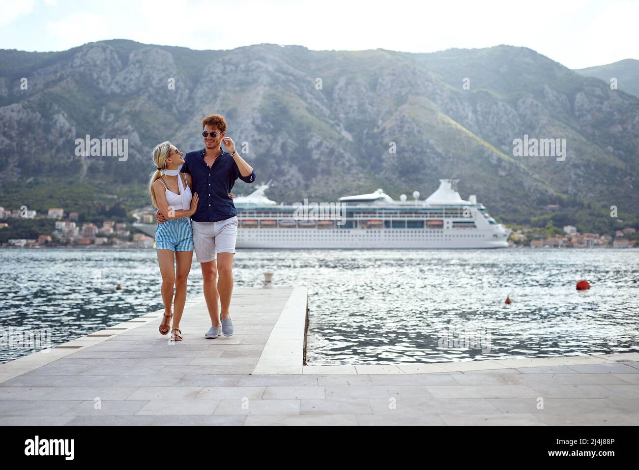 Elegant romantic couple walking on dock. Cruiser, city and mountains in ...