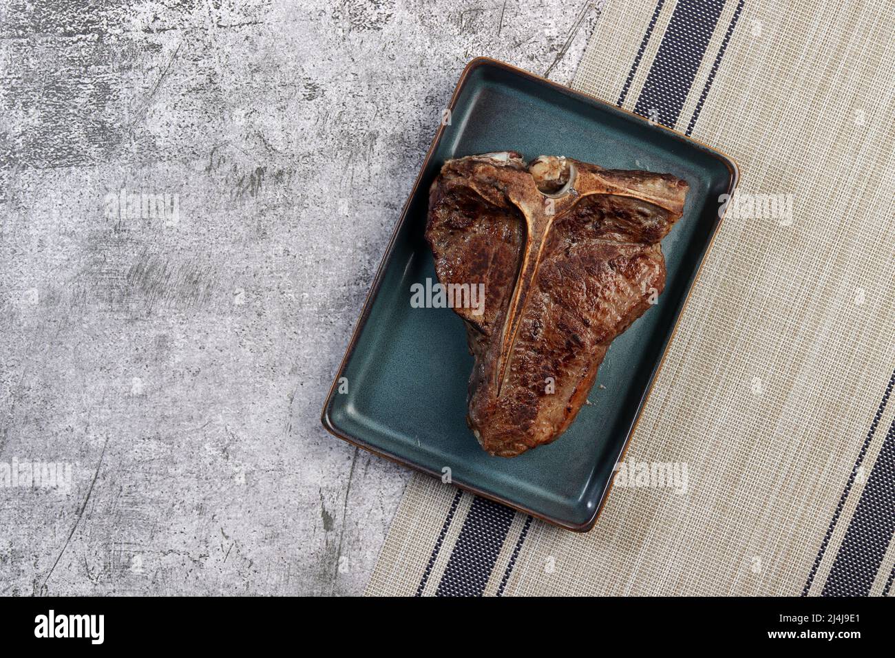 Roast T-bone steak on a rectangular plate on a dark background. Top ...