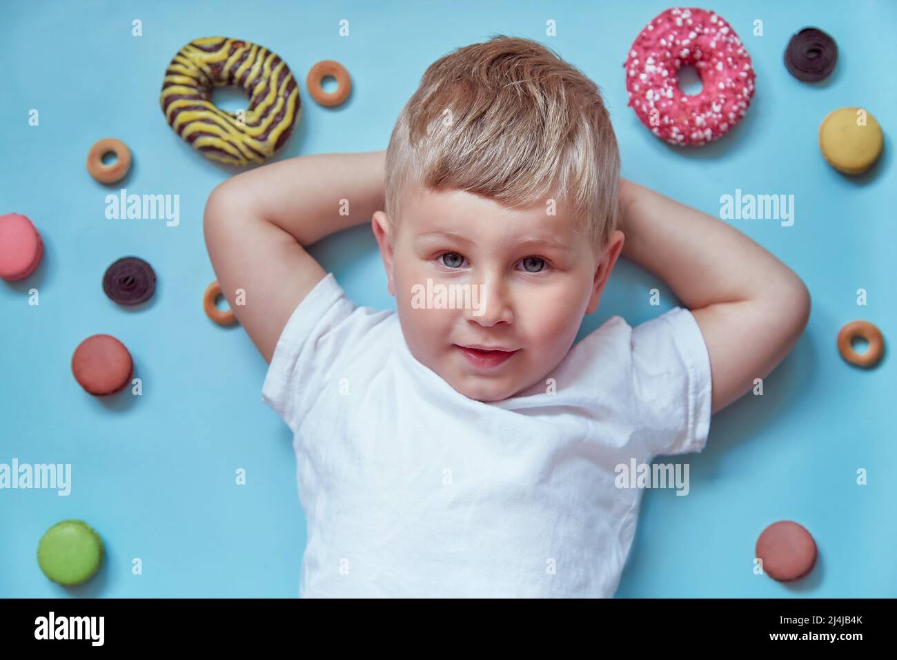 Cute smiling child on donuts and french macarons on blue background ...