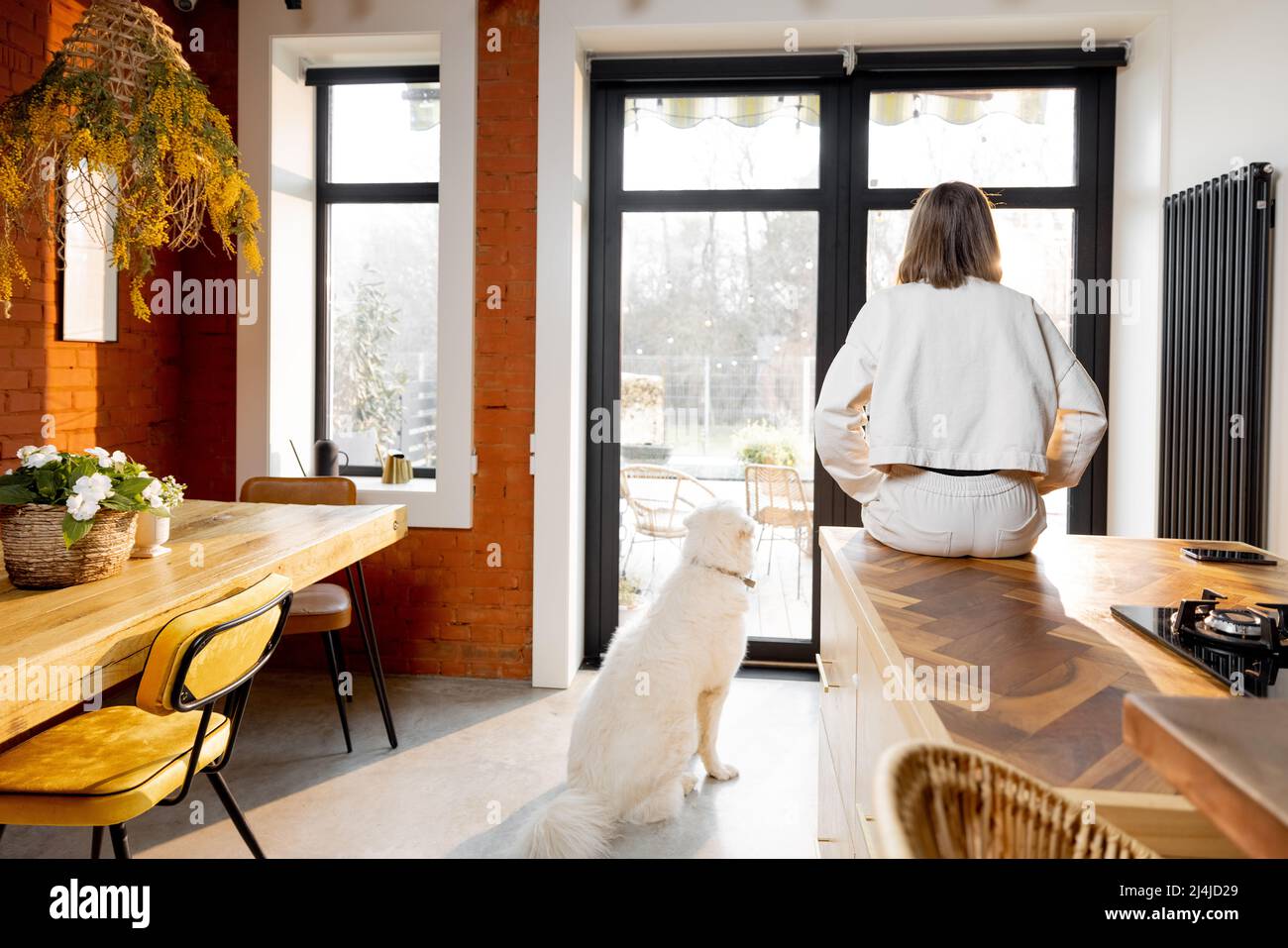 Woman sits alone on a kitchen table and looks out the windows at home ...