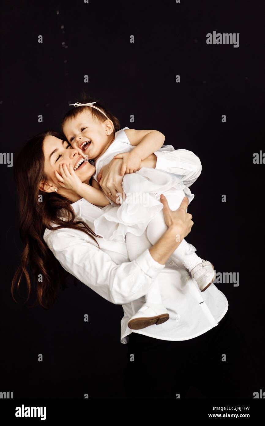 Happy brunette woman gently hugging beautiful baby girl, smiling. Attractive young mother ...