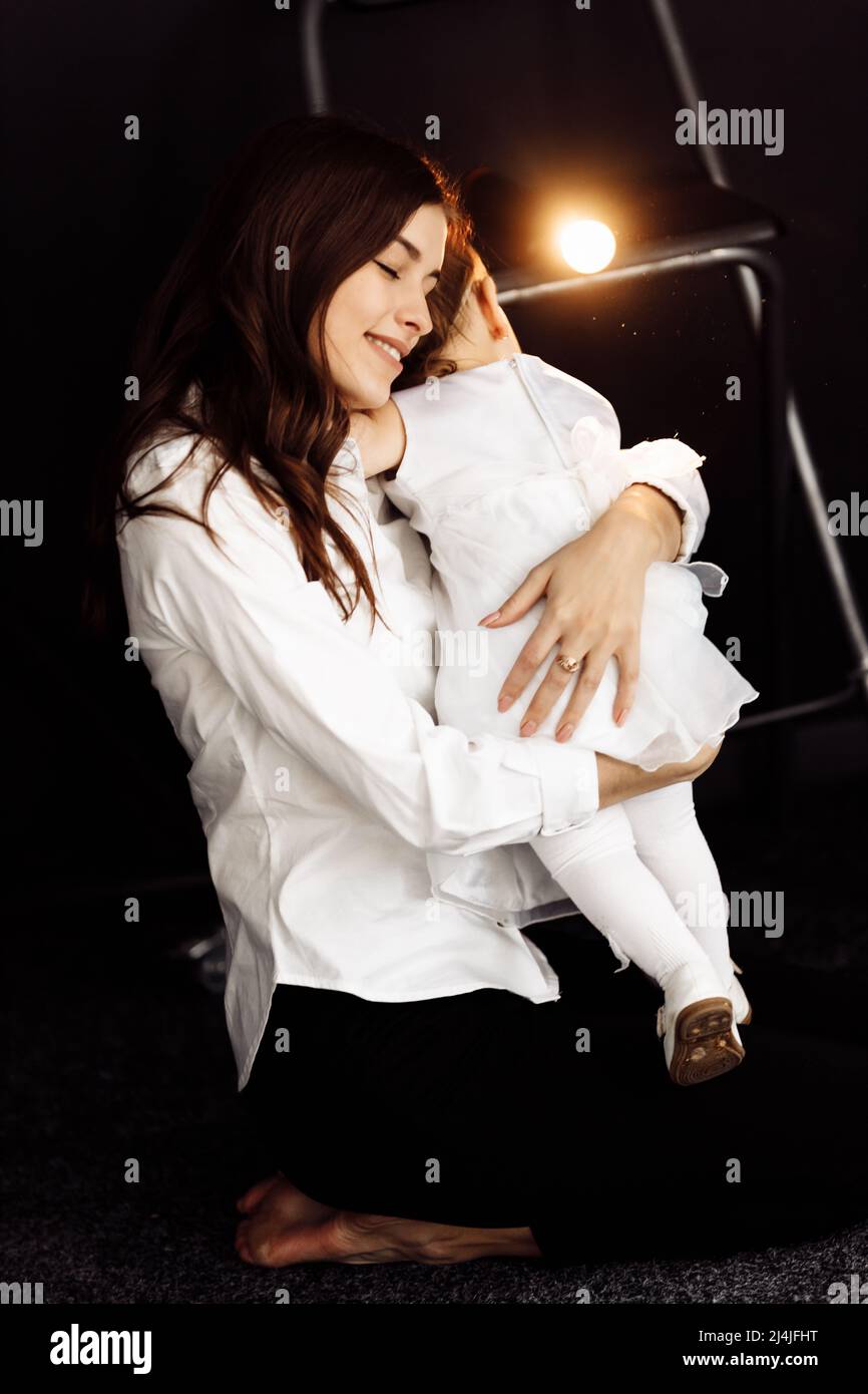 Dark-haired young mother gently holds in her arms and hugs little ...