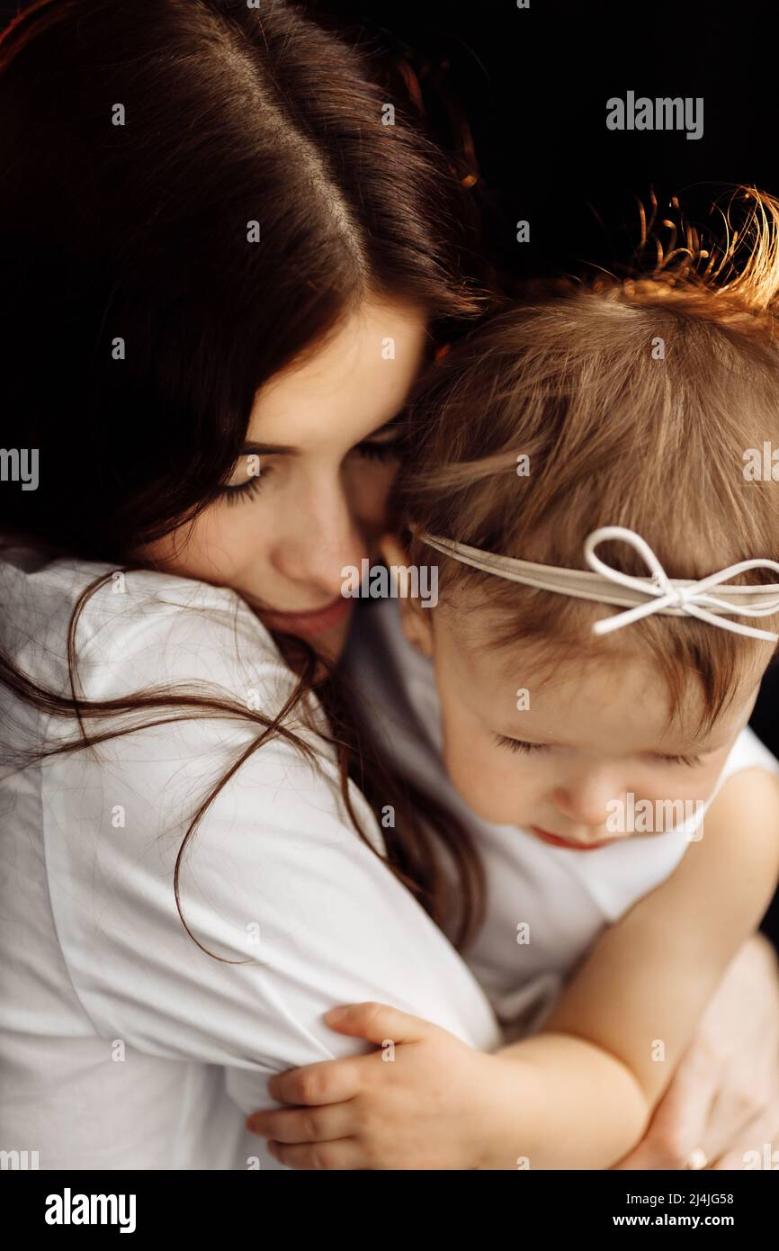 Dark-haired young mother gently holds in her arms and hugs little ...