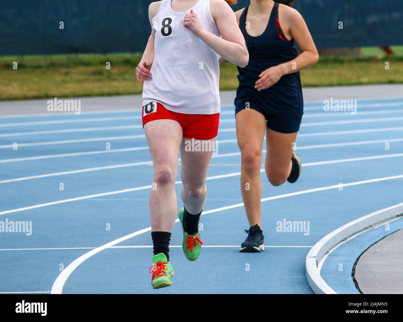 Front view of two high school girls running a race on a blue track ...
