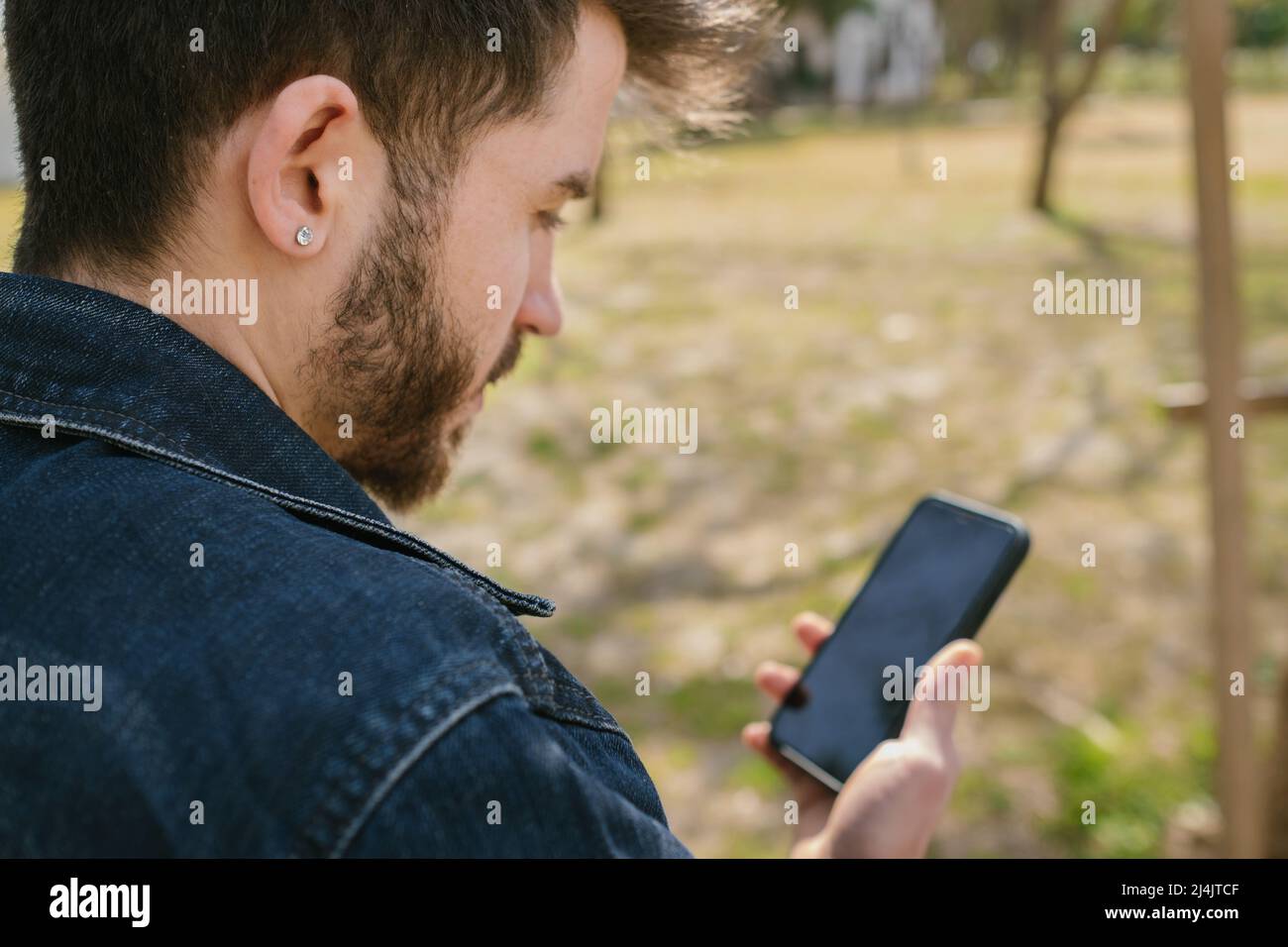 Young man looking at phone display, man in denim jacket looking at ...