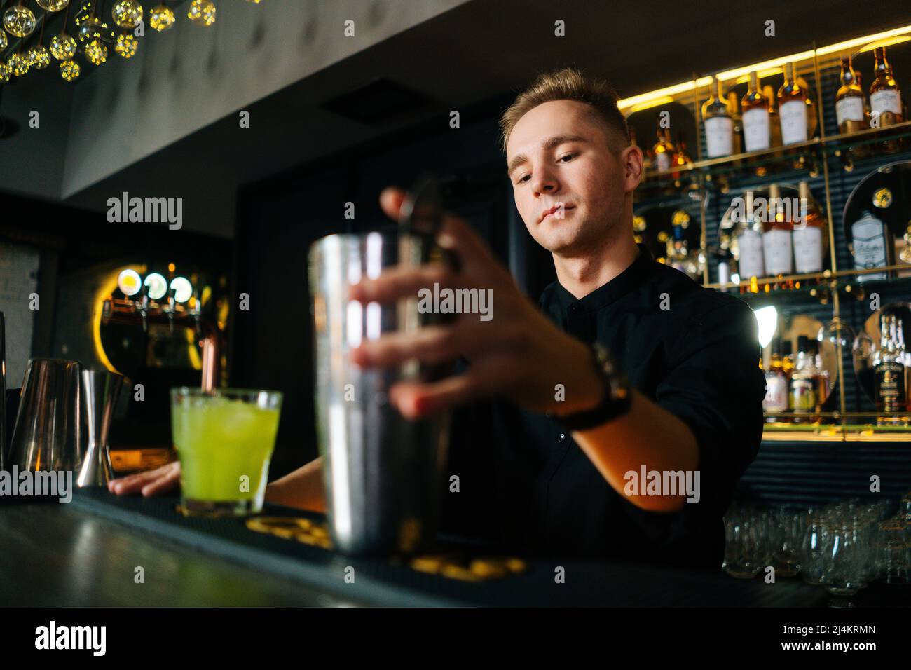 Low-angle view of confident bartender male making colorful alcoholic ...