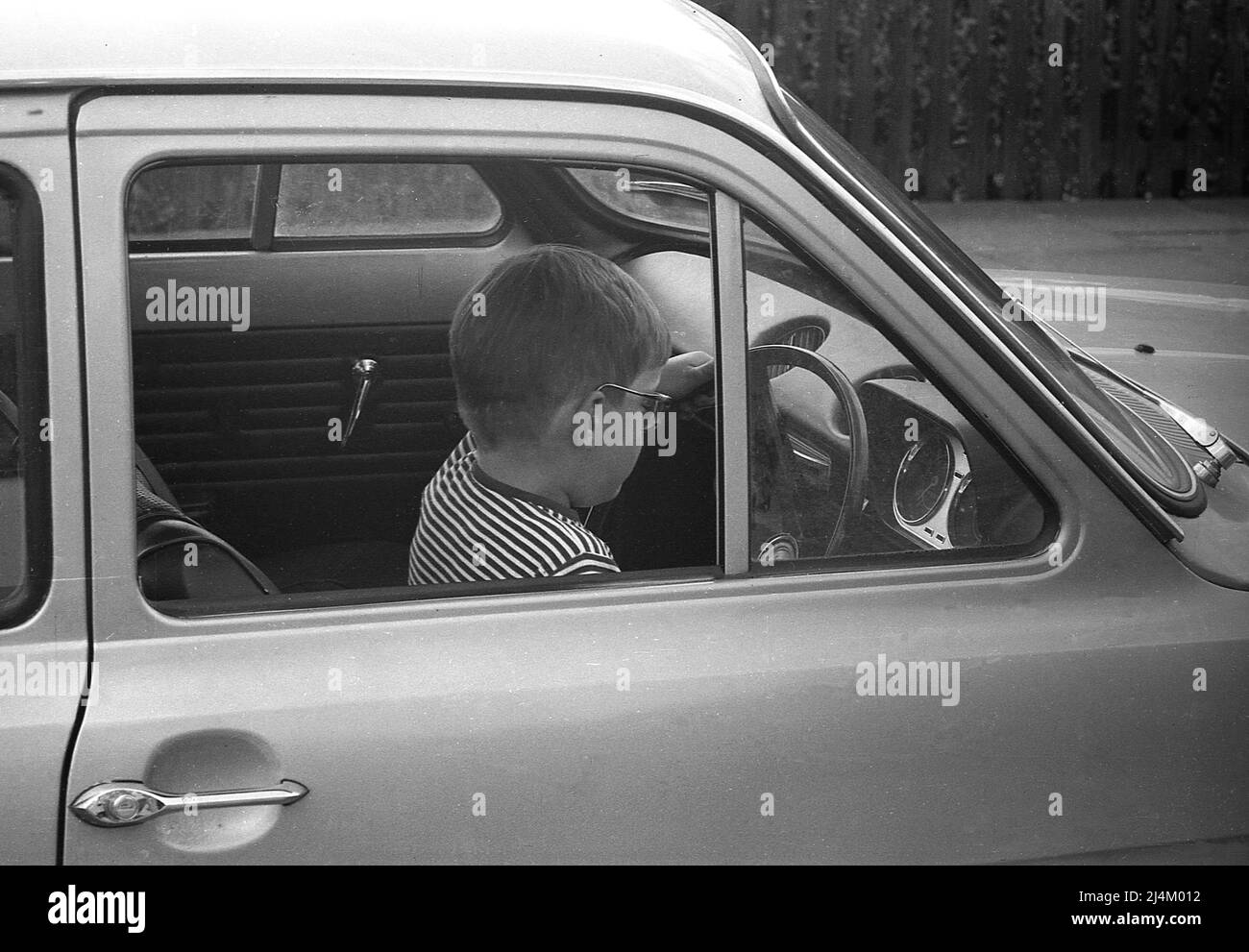 1970, historical, side view, a small boy sitting in the driver's seat ...